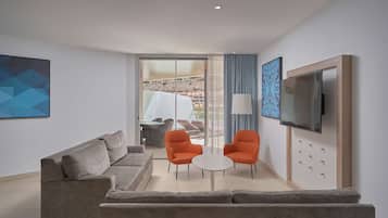 Uma sala de estar moderna com um sofá cinzento, duas poltronas laranja, uma mesinha branca, uma televisão e uma janela grande com vista para um edifício e uma montanha.
