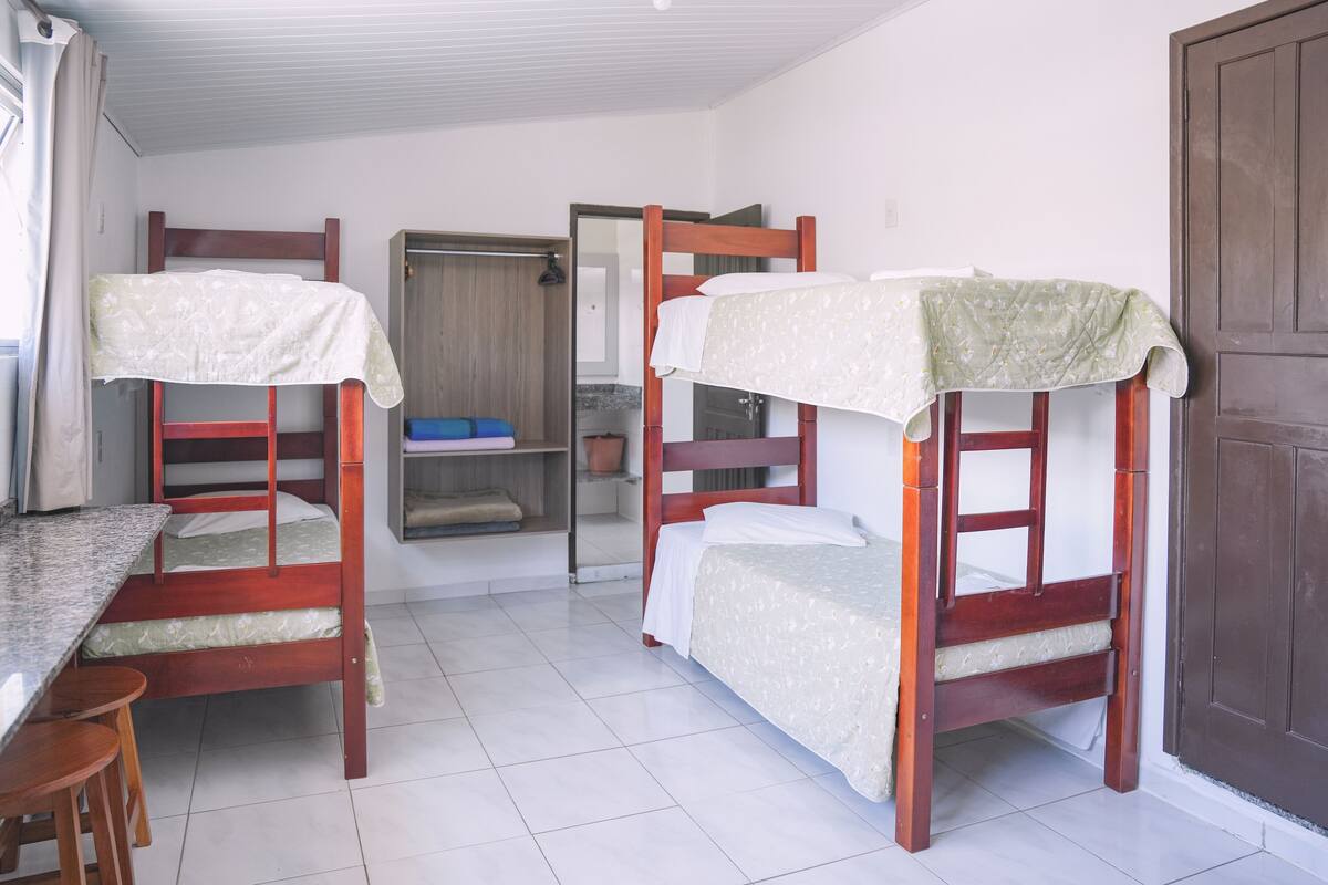 Quarto com beliches, uma mesinha e um guarda-roupa.