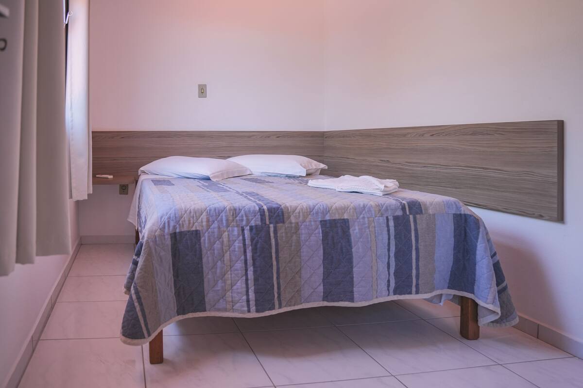 Uma cama de solteiro com cabeceira de madeira, colcha acolchoada e dois travesseiros.