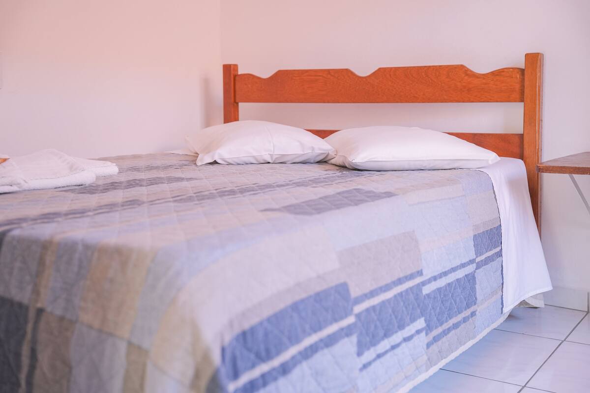 Uma cama com cabeceira de madeira, almofadas brancas e um edredom com padrão azul e branco.