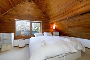 Quarto com painéis de madeira, uma cama grande, uma janela e uma mesa de cabeceira com abajur.