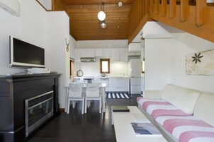 Uma sala de estar moderna com lareira, TV, sofá e área de jantar com cadeiras e mesa.