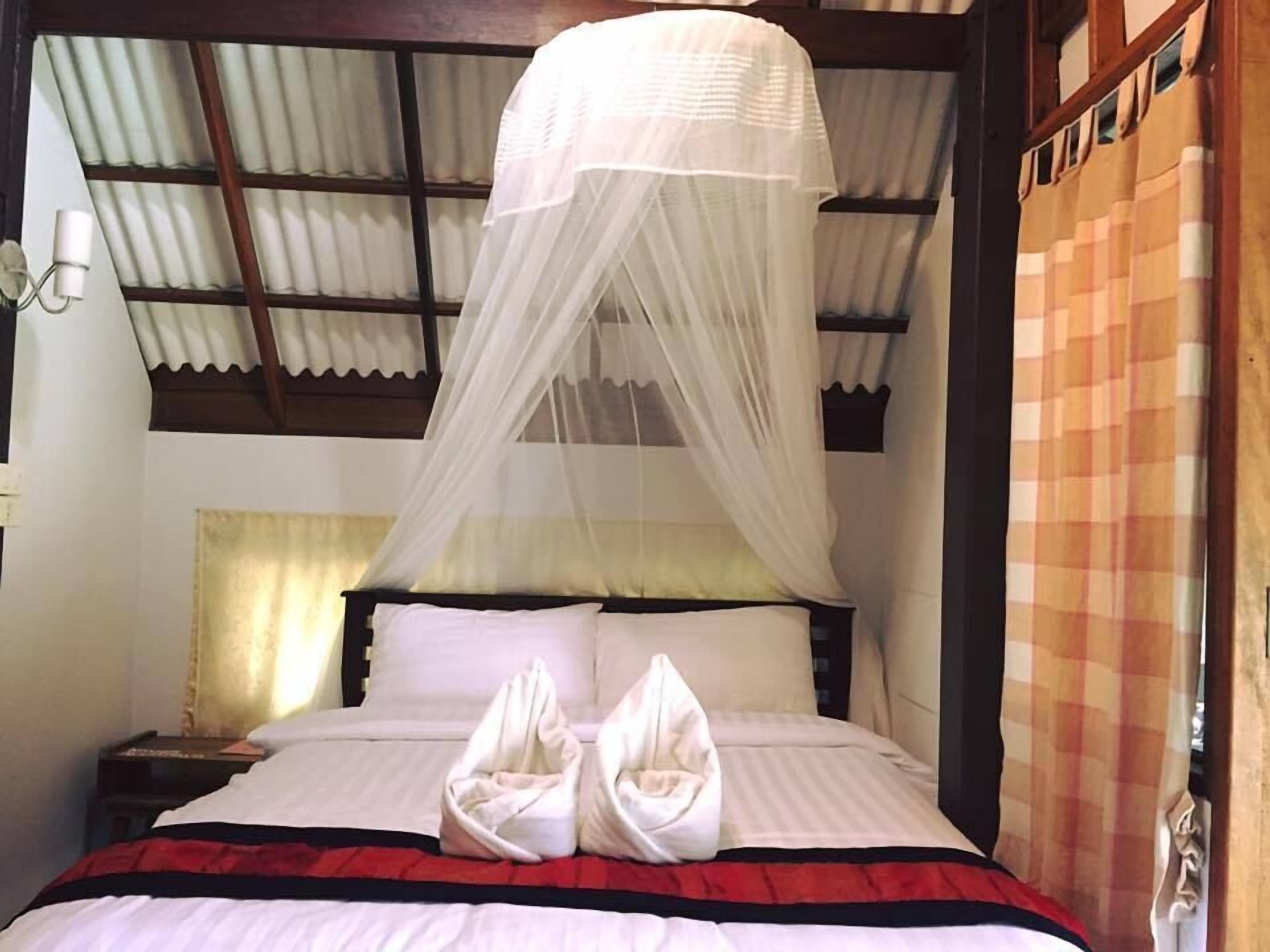 Uma cama com dossel branco, duas almofadas e um edredom listrado em vermelho e preto.