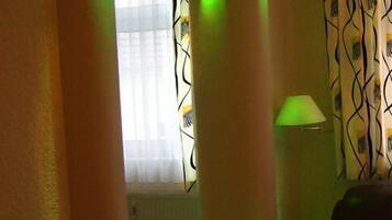 Um quarto com janela, luminária e sofá.