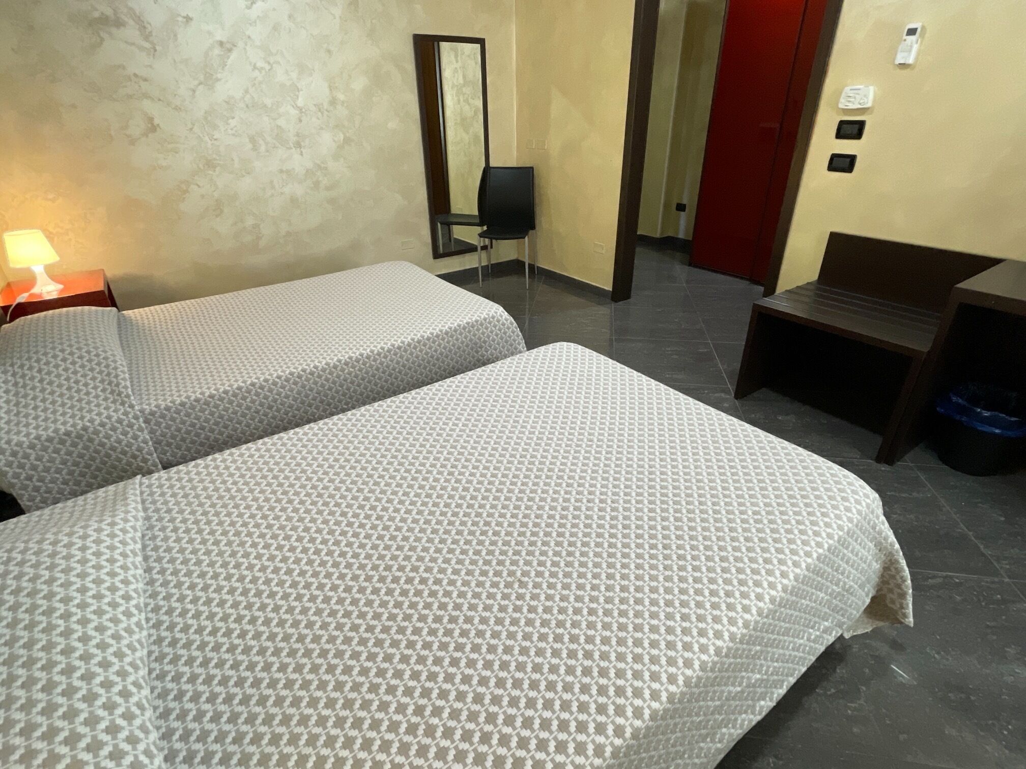 Quarto de hotel com duas camas, televisão, escrivaninha e espelho.