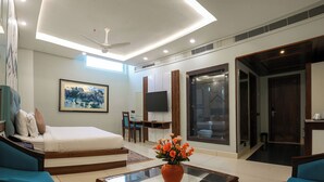 Quarto de hotel moderno com cama, sofá, televisão e banheiro com porta de vidro.