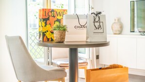 Uma mesa com sacolas de compras da Louis Vuitton e Chanel, uma cadeira e um vaso de planta.