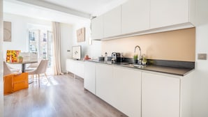Cozinha moderna com armários brancos, bancada preta e área de refeições com mesa e cadeiras.