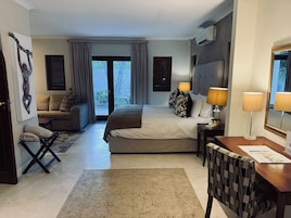 Quarto de hotel moderno com uma cama grande, um sofá, uma escrivaninha com abajur e vista para o exterior por uma porta deslizante.