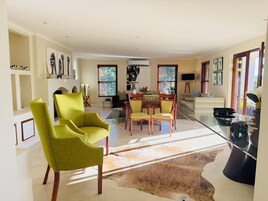 Uma sala de estar espaçosa com uma grande poltrona verde, uma área de refeições com cadeiras estampadas e uma mesa de centro de vidro.