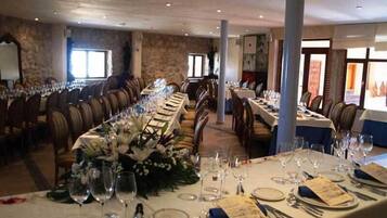 Uma sala de banquetes com longas mesas preparadas para refeições, com centros de mesa florais e impecáveis arranjos de mesa.