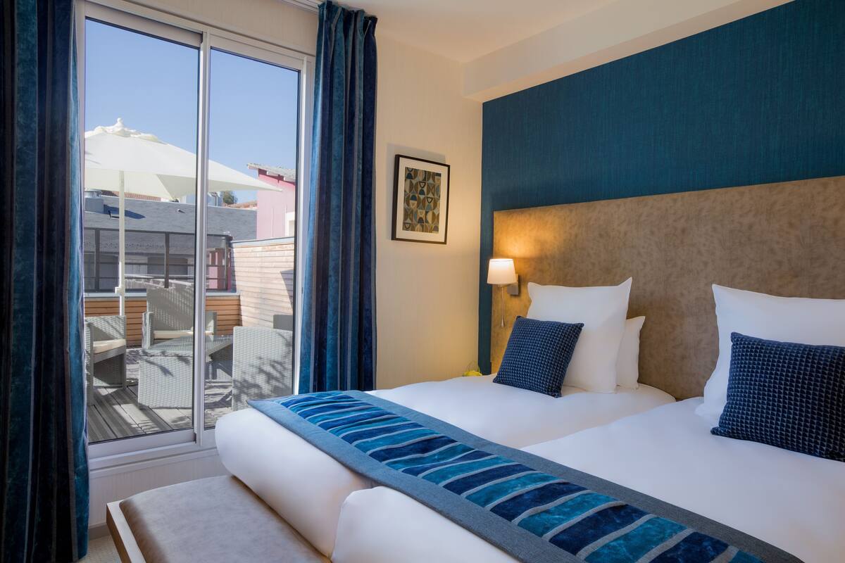Quarto de hotel com uma cama grande, vista para a área externa e uma janela com cortinas.