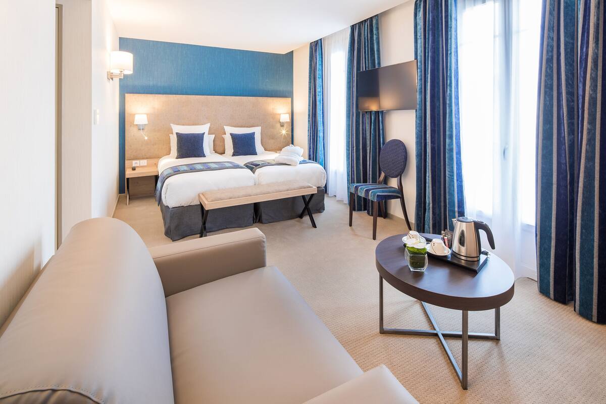 Quarto de hotel com cama, sofá, mesinha com chaleira e televisão.