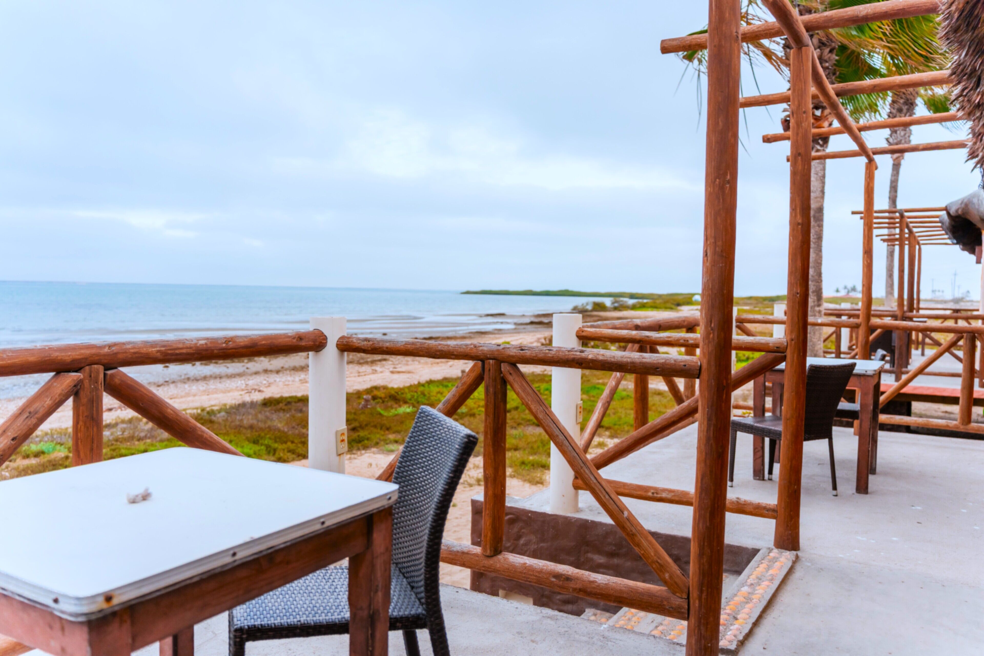 Um restaurante à beira-mar com mesas ao ar livre, vista para o mar e estrutura de madeira.