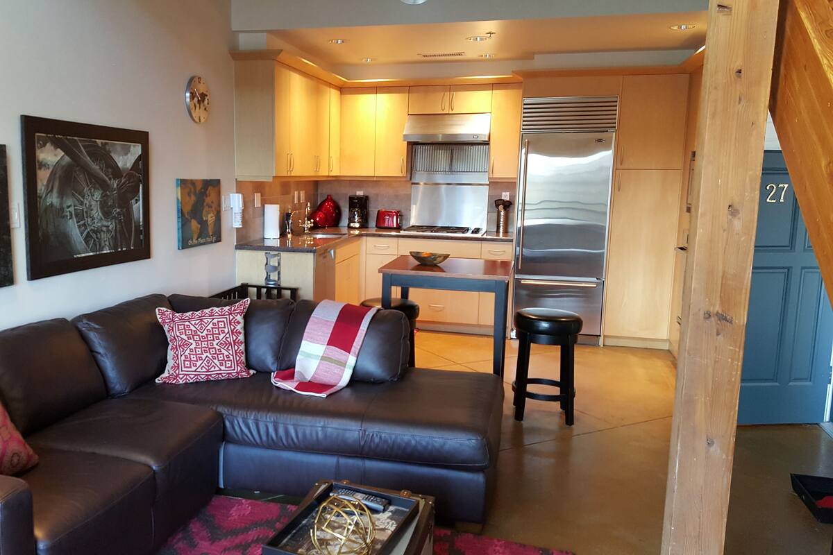 Uma sala de estar moderna com um sofá de couro, uma mesa de centro e uma área de cozinha com armários de madeira e eletrodomésticos de aço inoxidável.
