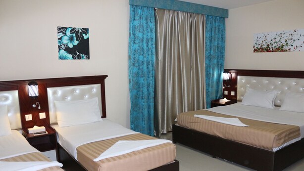 Quarto de hotel com três camas, uma janela grande com cortinas azuis e uma obra de arte pendurada na parede.