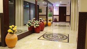 Um saguão de hotel com piso de mármore, grandes vasos de plantas e um espelho refletindo o ambiente.