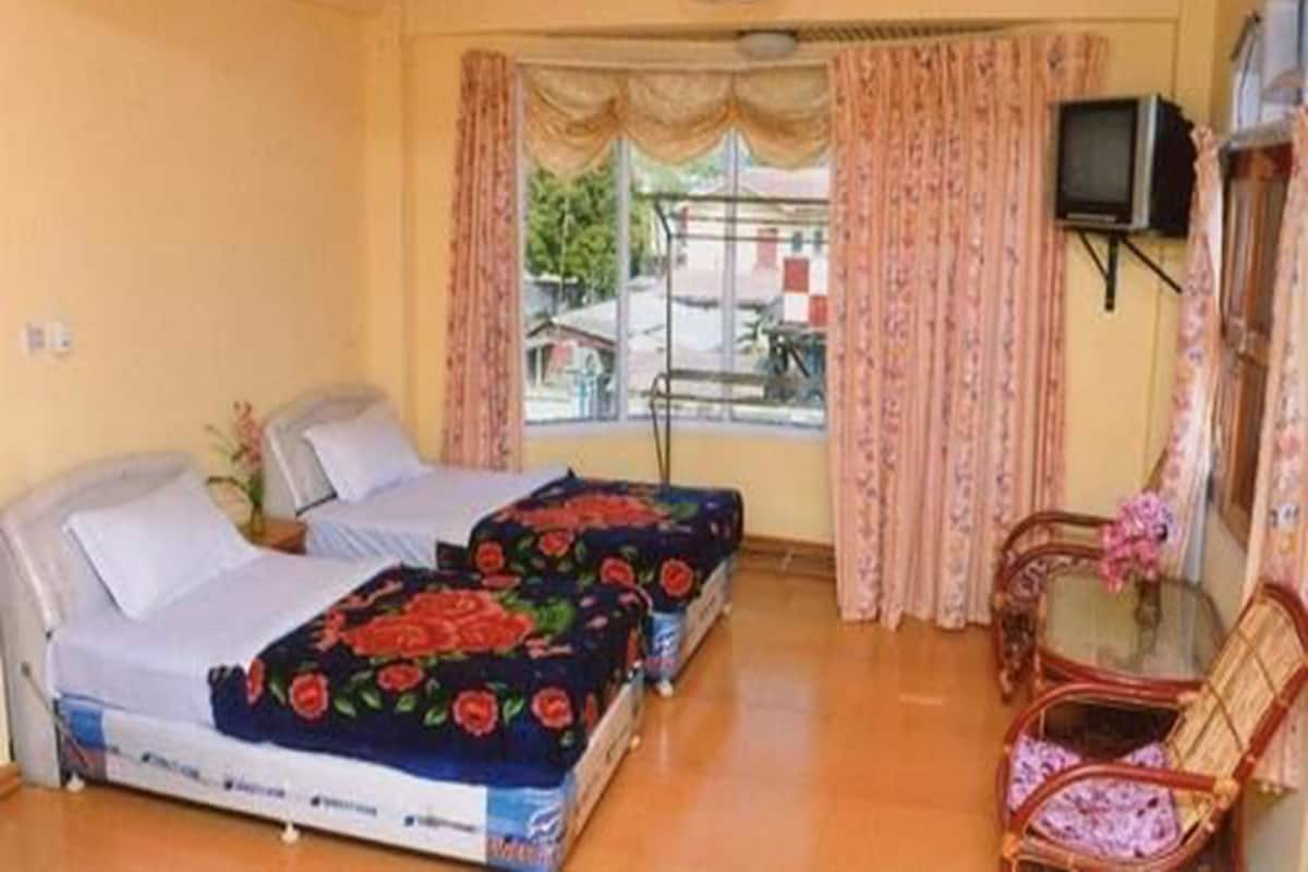 Quarto de hotel com duas camas, televisão, janela com cortinas e uma cadeira.