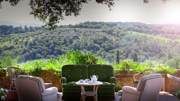 Um sofá verde e duas cadeiras em um deck de madeira com uma mesa, com vista para um vale exuberante.