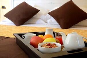 Uma bandeja de café da manhã com frutas, um jarro, uma xícara e uma tigela sobre a cama, com travesseiros.