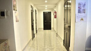 Um corredor com piso ladrilhado, uma porta preta no final e um extintor de incêndio na parede.