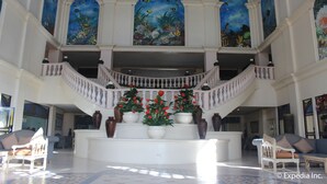Um hall imponente com uma escadaria central, plantas em vasos e um mural retratando uma cena subaquática.