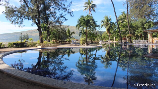 Piscina com água cristalina refletindo árvores e uma montanha ao fundo.