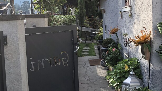 Uma entrada protegida por portão para um terreno, com um caminho de pedra que leva a um alpendre.