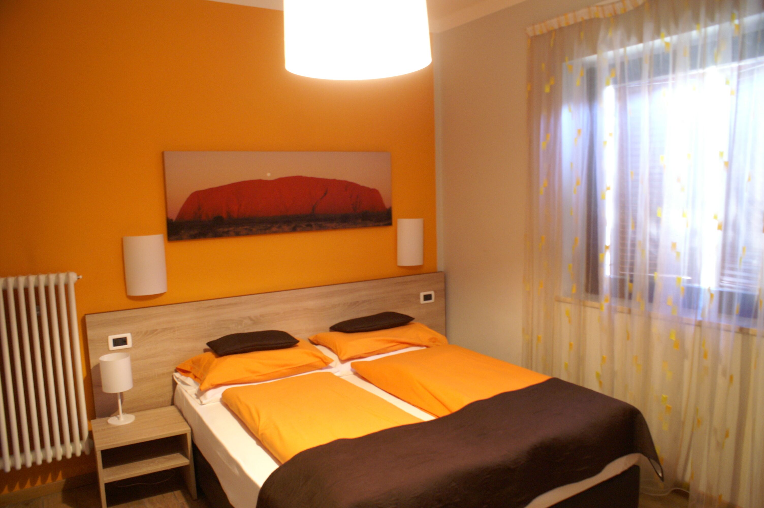Quarto de hotel com cama, mesa de cabeceira, abajur, um quadro na parede e janela com cortinas.
