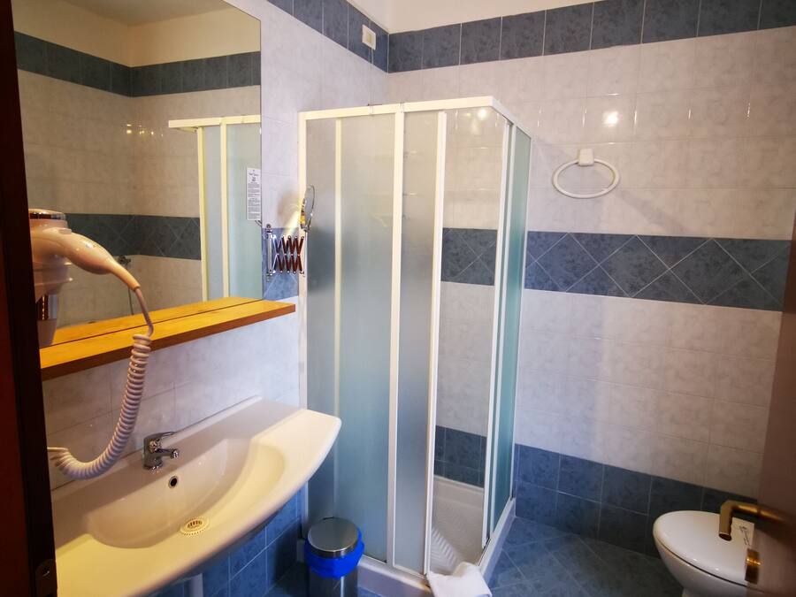 Casa de banho com chuveiro em cabine de vidro, lavatório com espelho e sanita.