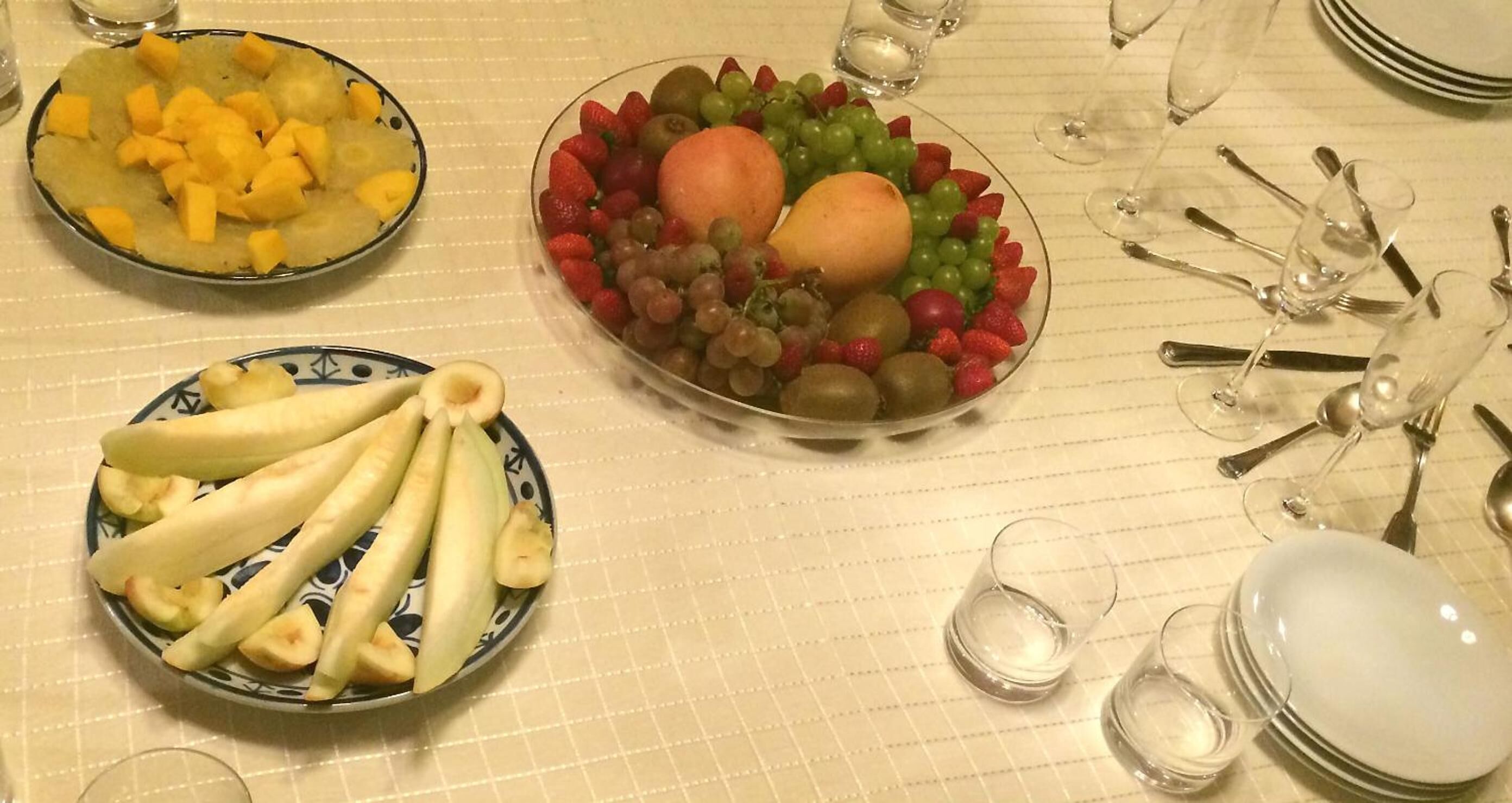 Uma mesa posta com pratos de fruta, copos e talheres.