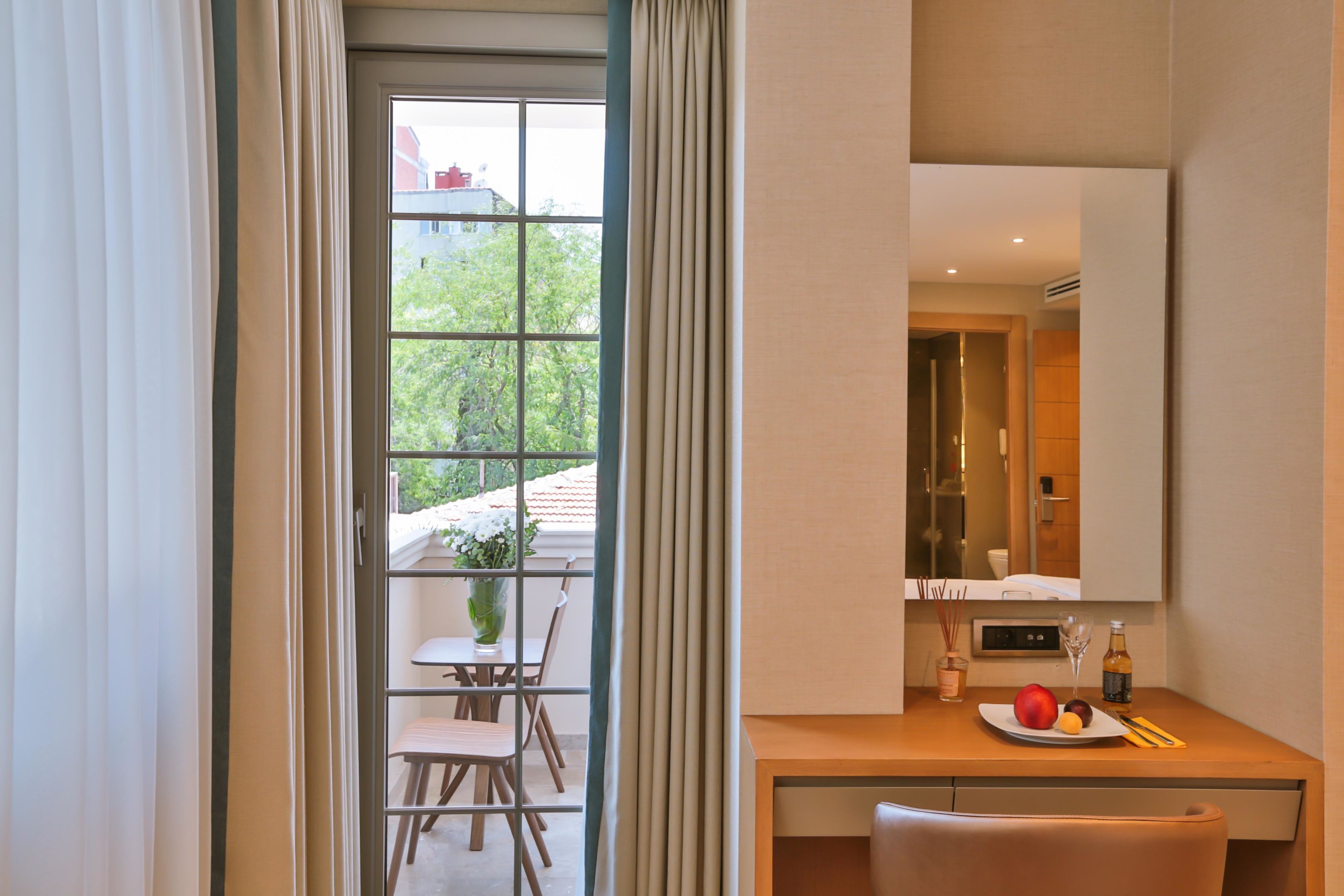 Quarto de hotel com vista para uma varanda, um espaço de refeições e uma mesa com uma tábua de fruta e uma garrafa.