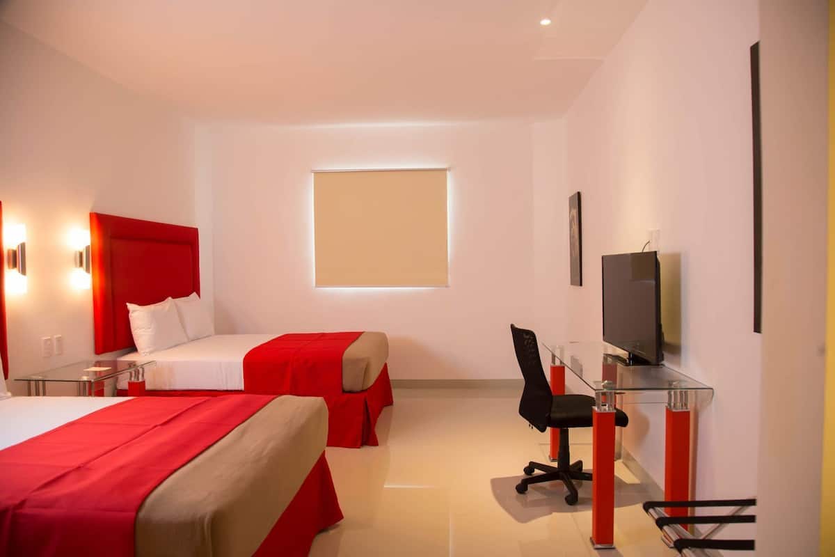 Quarto de hotel com duas camas, uma escrivaninha, uma cadeira, uma televisão e uma janela.