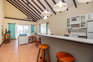 Cozinha com ilha central, banquetas, ventilador de teto e vista para o oceano.