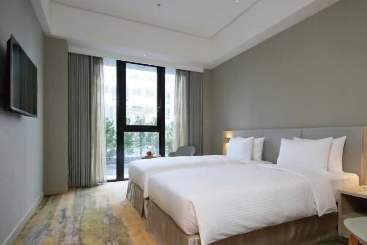 Quarto de hotel com uma cama grande, uma escrivaninha, uma cadeira e uma janela com cortinas.