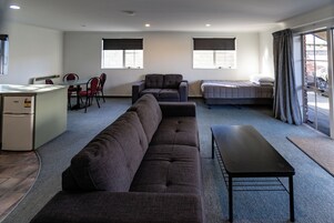 Quarto com sofá, mesa de jantar com cadeiras, cama e pequena cozinha.