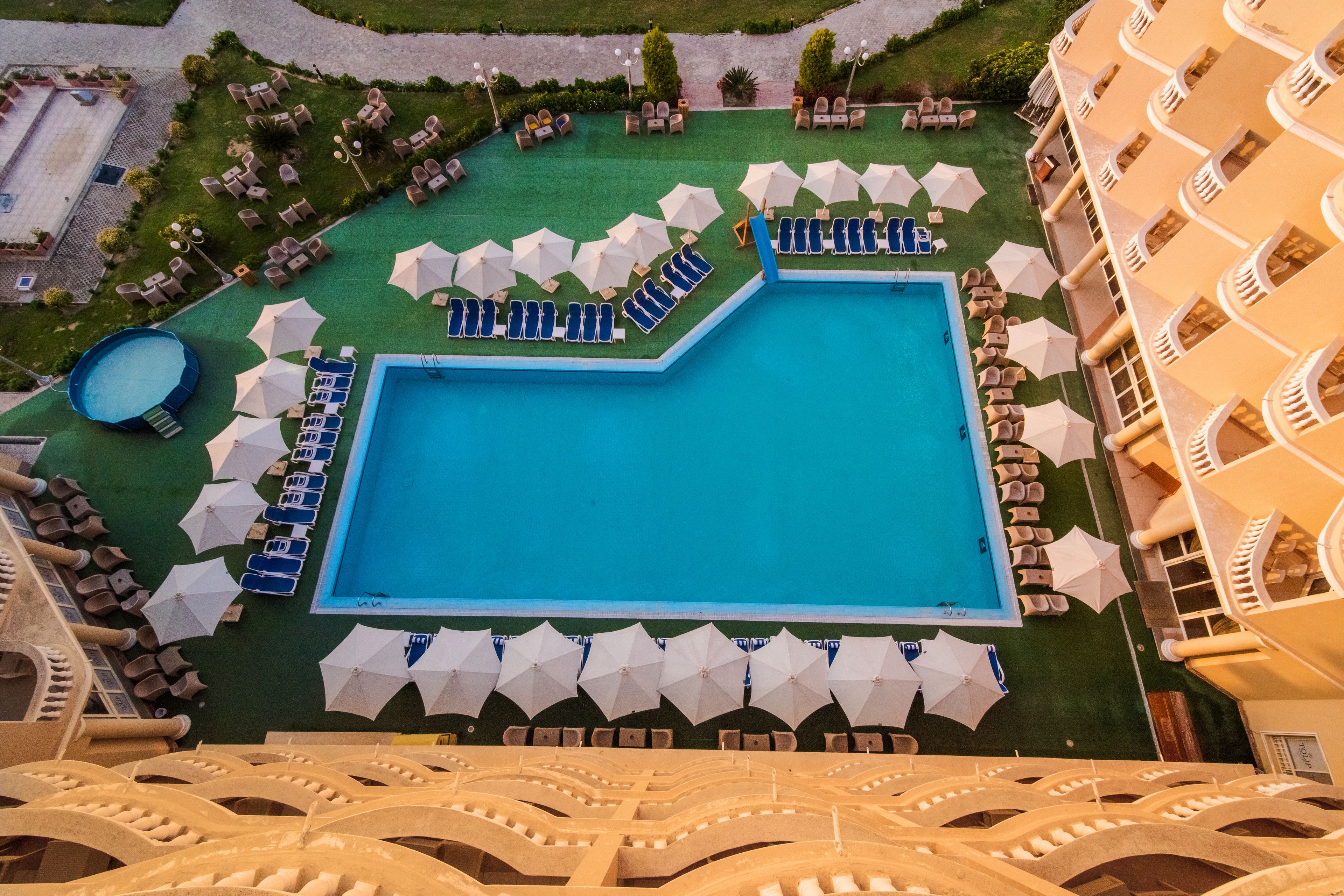 Uma área de piscina no terraço, com várias espreguiçadeiras e guarda-sóis, cercada por uma piscina e um edifício com varandas.