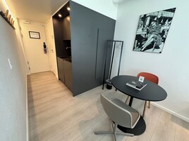 Quarto compacto com mesa de jantar, uma cadeira, lixeira pequena e uma foto emoldurada na parede.