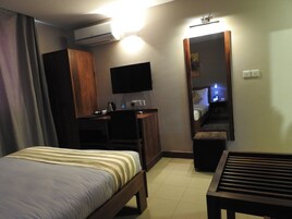Quarto de hotel com cama, escrivaninha, cadeira, televisão, espelho e mesa pequena.