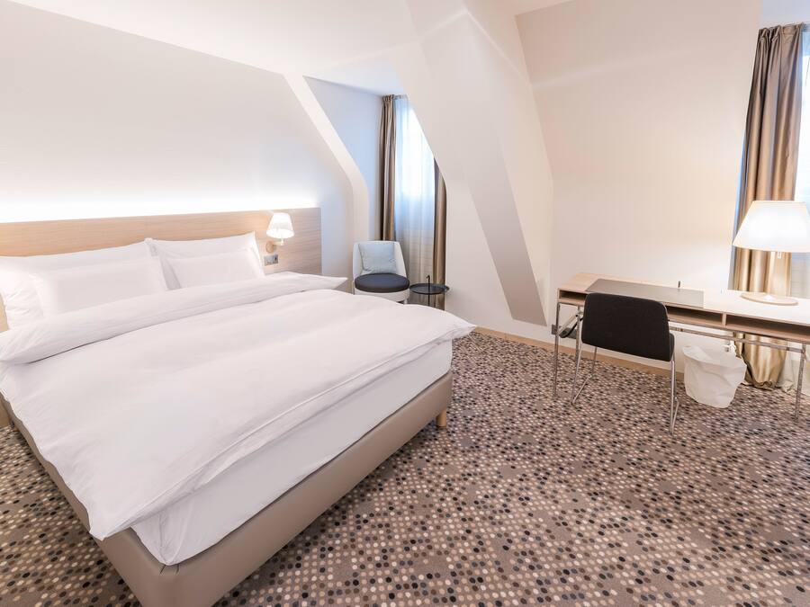 Quarto de hotel com uma cama grande, uma escrivaninha, uma cadeira e uma pequena mesa.