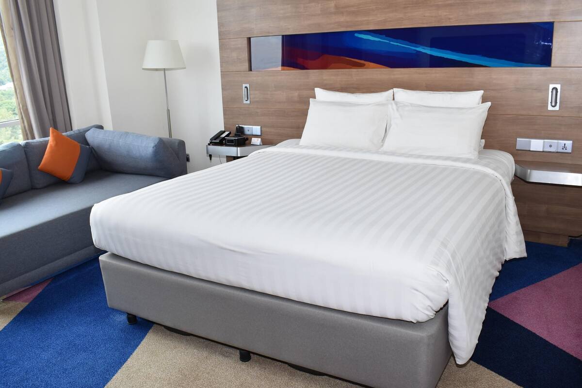 Quarto de hotel com uma cama grande, um sofá, uma mesa de cabeceira e uma obra de arte pendurada na parede.
