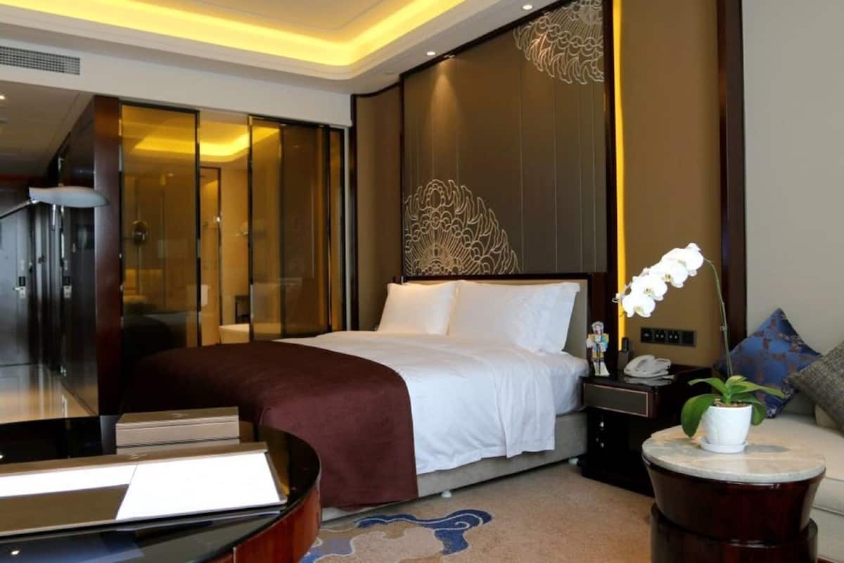 Quarto de hotel moderno com uma cama grande, uma escrivaninha, chuveiro com box de vidro e um painel decorativo na parede.
