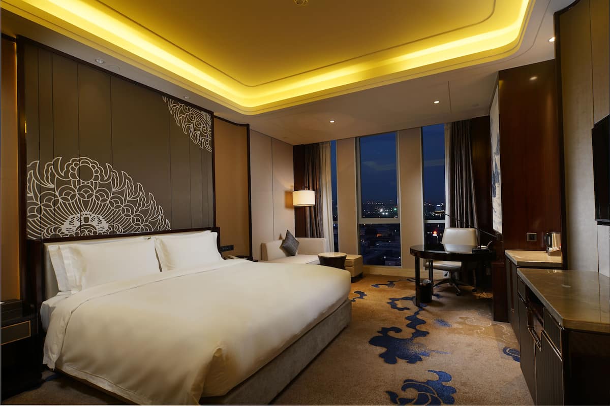 Quarto de hotel com uma cama grande, uma escrivaninha e vista para a cidade à noite.