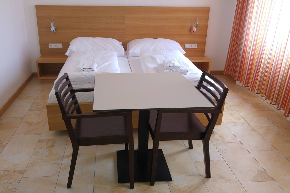 Quarto com cama, mesas de cabeceira, uma mesa e cadeiras.