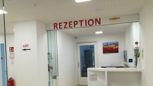 Uma área de recepção com um letreiro 'RECEPTION', um letreiro 'LIFT', um extintor e uma divisória de vidro.