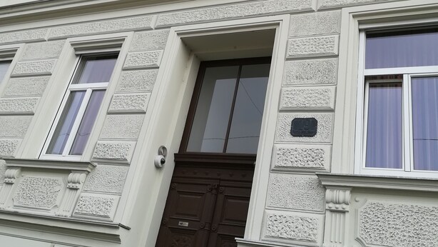 Um edifício com vários andares e detalhes arquitetónicos elaborados, incluindo molduras decorativas e uma grande porta de entrada central.