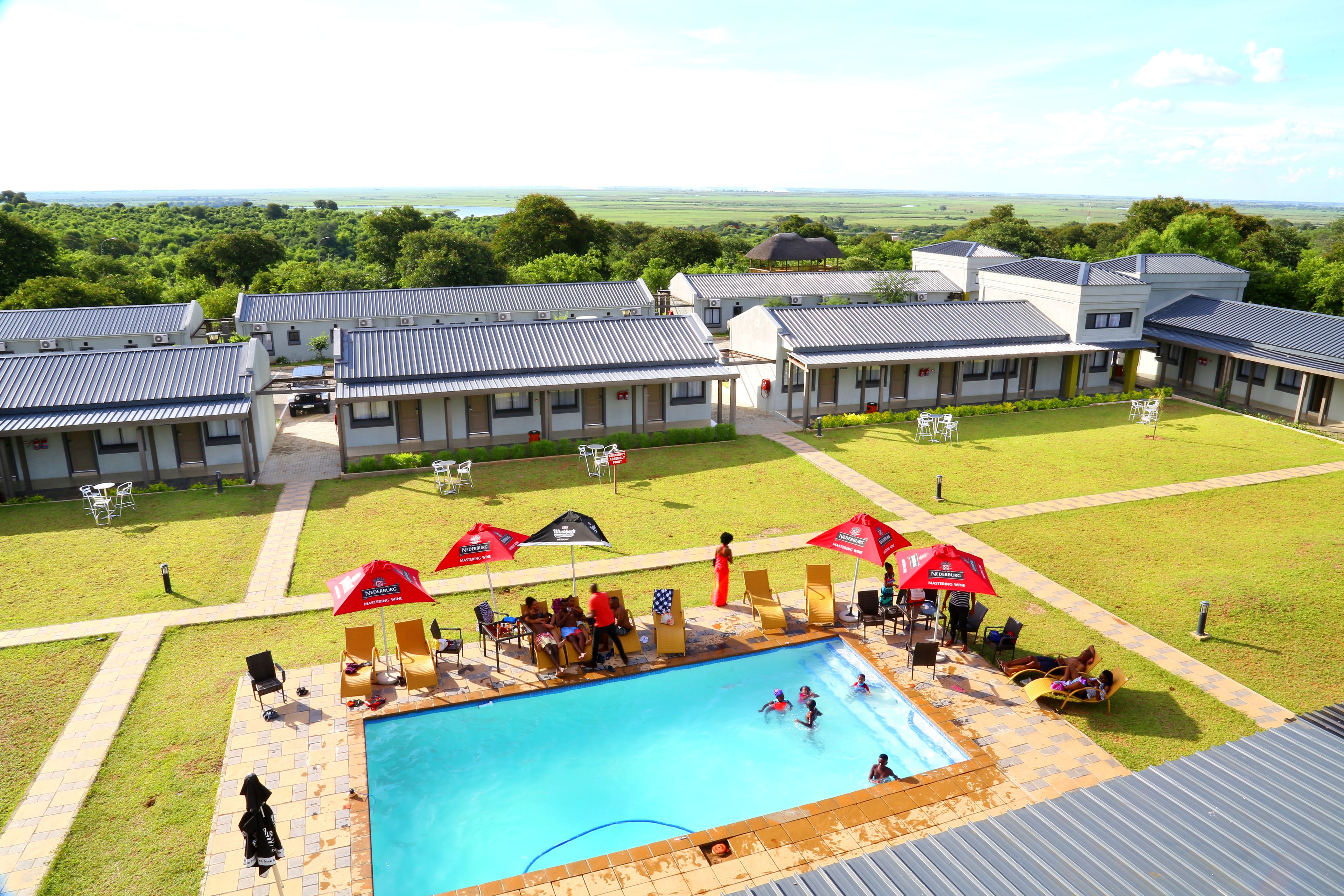 Uma área de piscina com espreguiçadeiras e guarda-sóis, cercada por edifícios de hotel com vista para o campo.