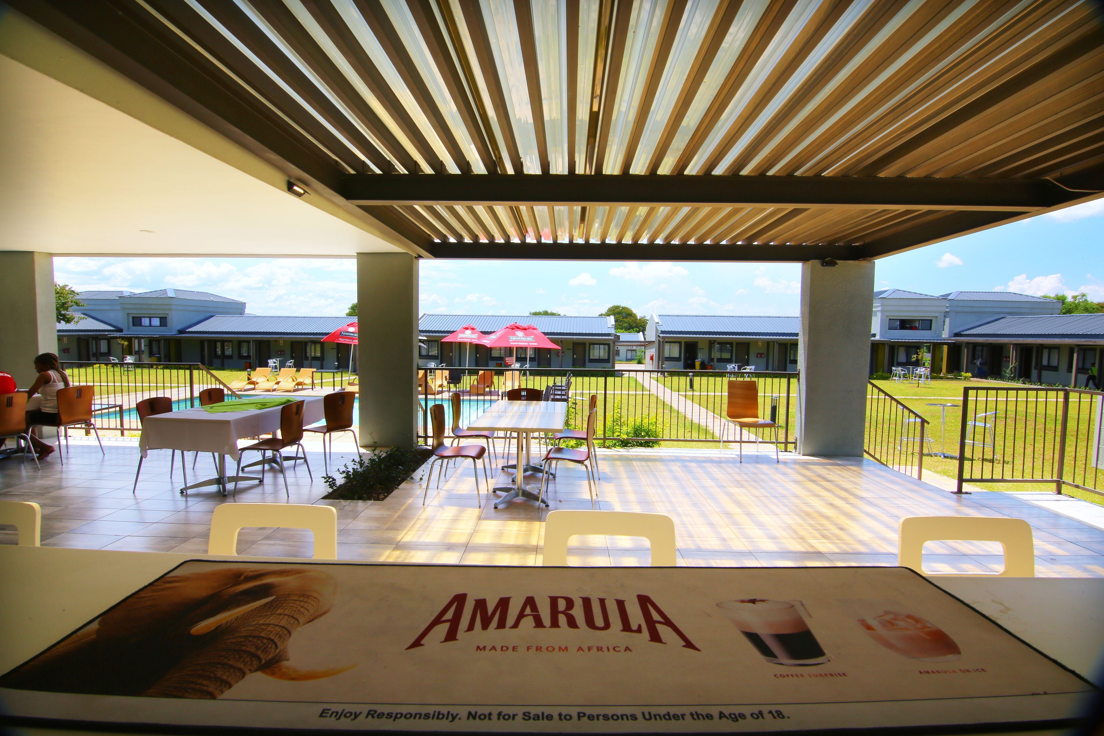 Uma área de estar ao ar livre com mesas e cadeiras, uma piscina ao fundo e vista para edifícios.