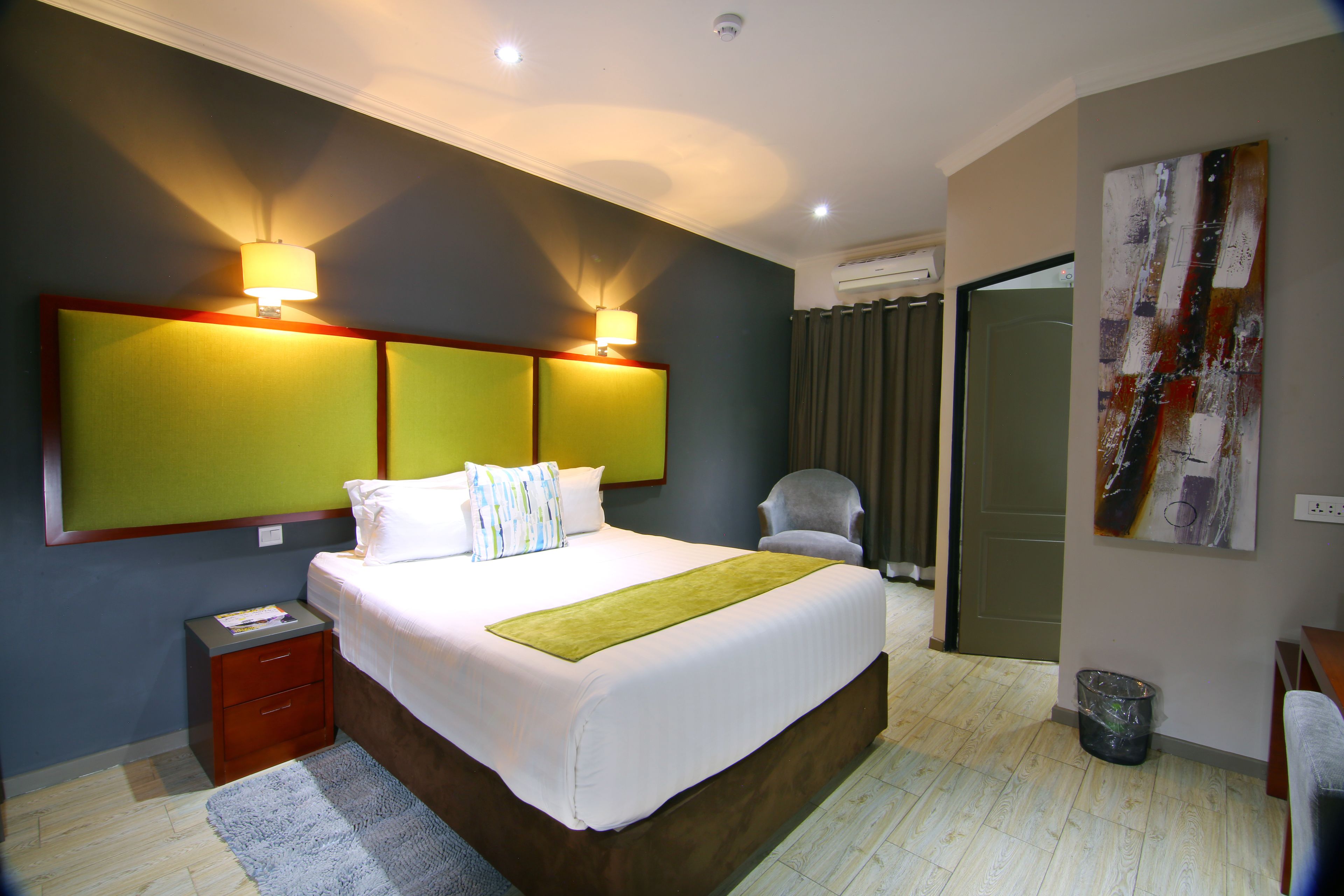 Quarto de hotel com uma cama grande, mesas de cabeceira, uma cadeira, um quadro e um ar condicionado.
