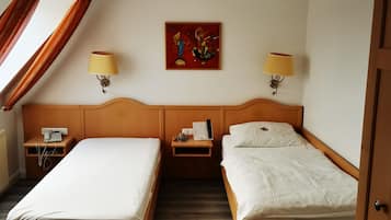 Quarto de hotel com duas camas de solteiro, uma mesinha de cabeceira com abajur, um telefone e um quadro na parede.